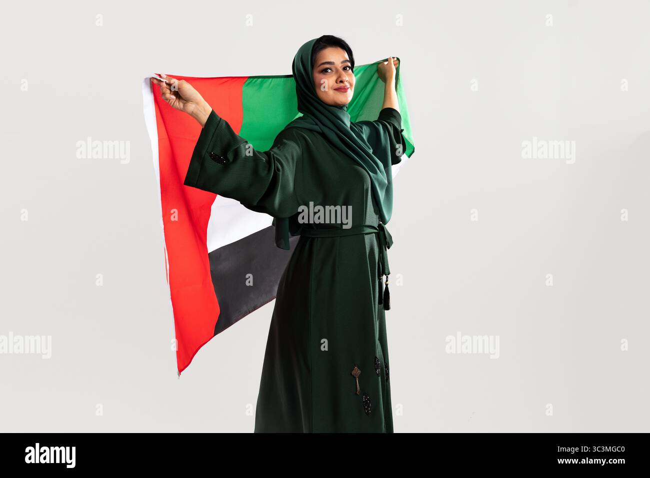 Emirati woman wearing a traditional green abaya and hijab proudly holds ...