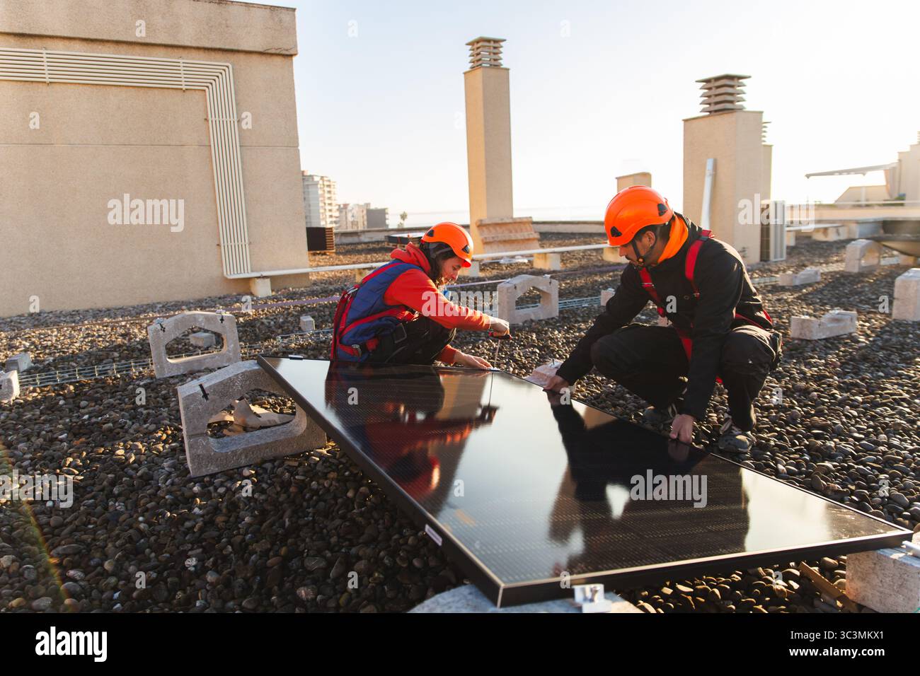 Workers wearing safety gear install solar panels on a rooftop ...