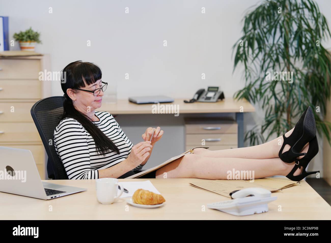 Secretary files her nails and has placed her feet on the desk Stock ...