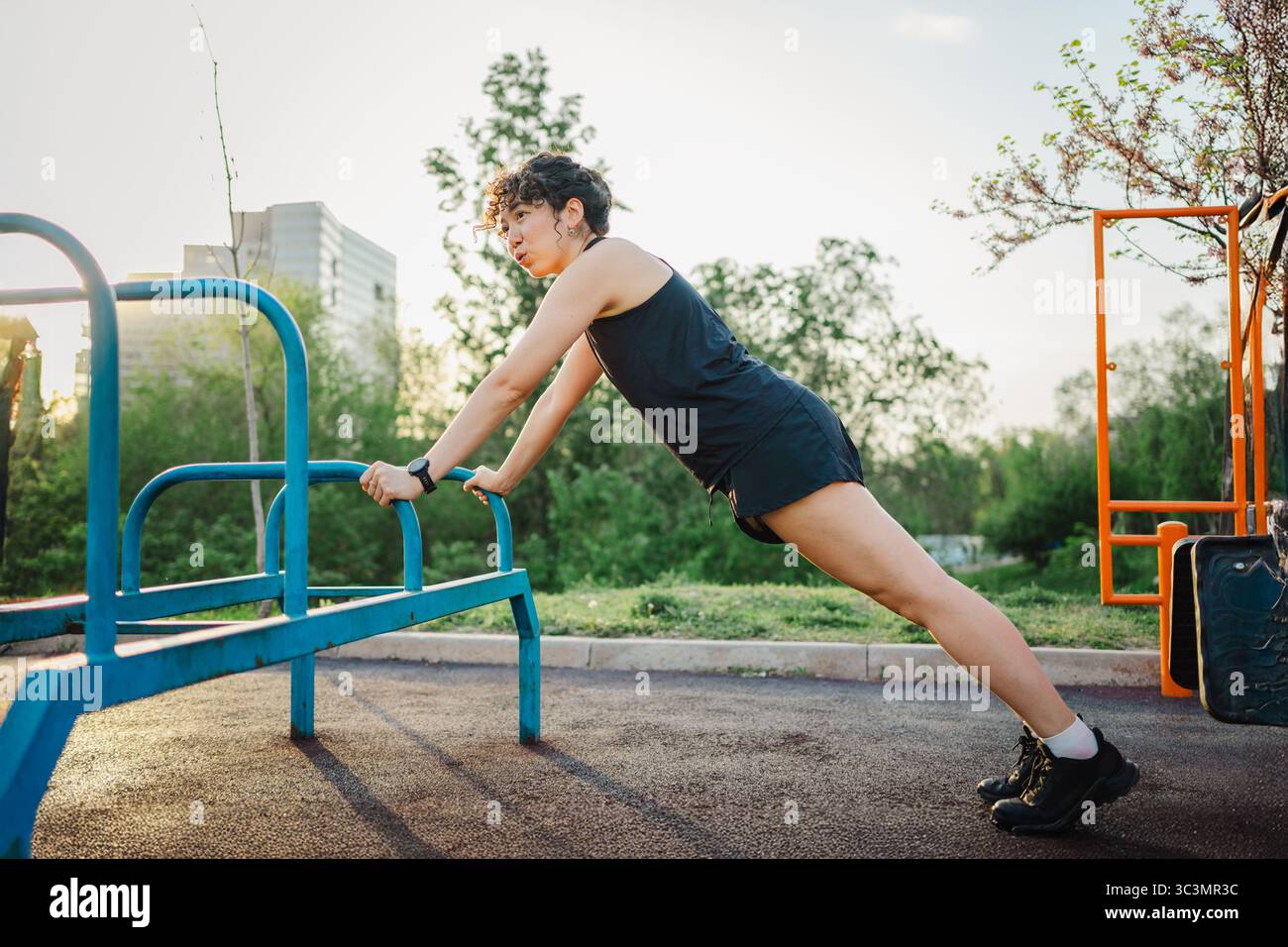 A young curly-haired woman engages in a push-up workout outdoors, using ...