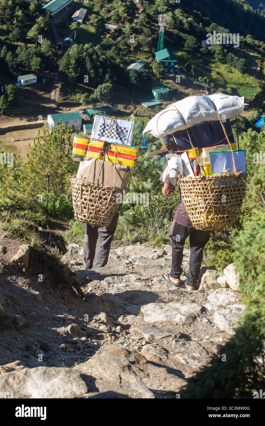 Porters carry heavy loads down a rugged path in Namche Bazaar, Nepal ...