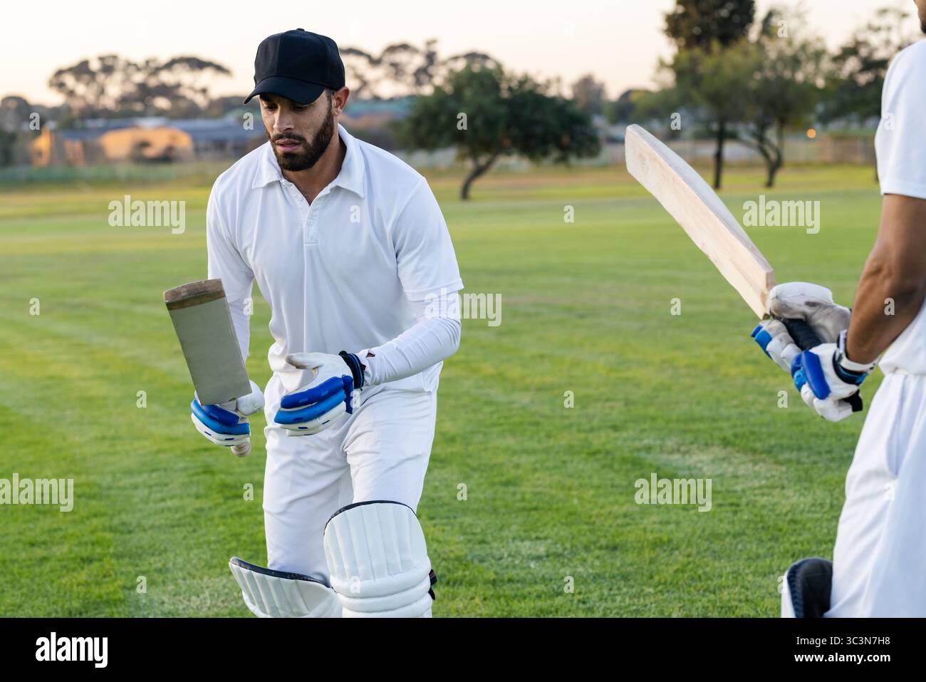 Asian male teammates practicing cricket on field wearing white uniforms ...