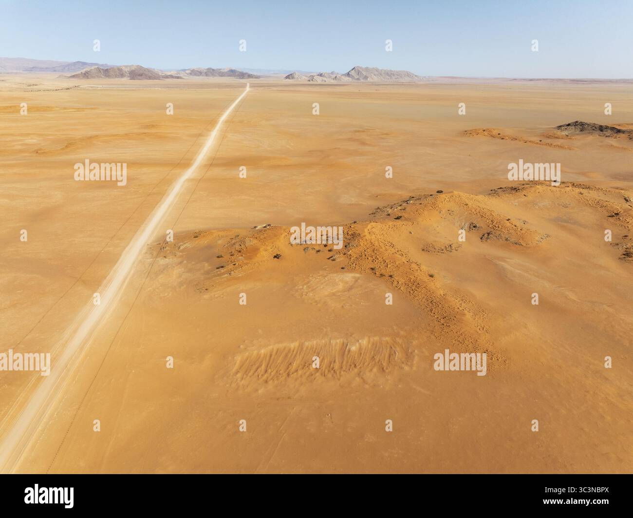 Aerial view of a stark, sandy landscape cut by a straight road leading ...