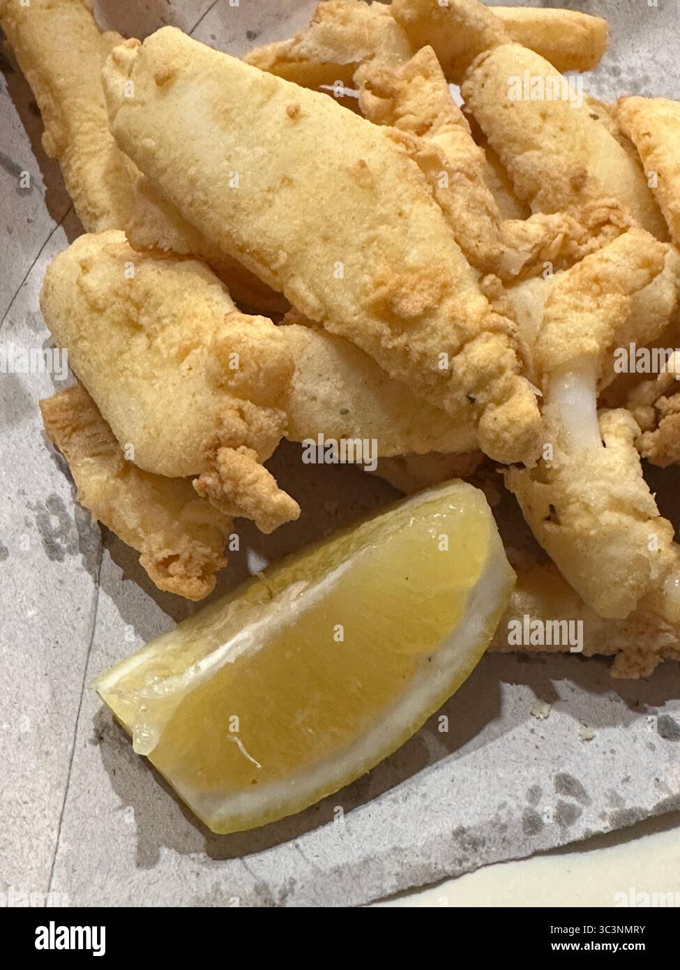 Fried cuttlefish on a paper with a lemon slice Stock Photo - Alamy
