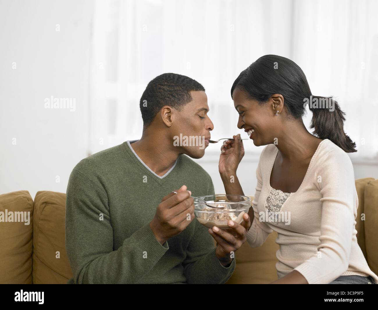 A young Black couple shares a playful and intimate moment while eating ...