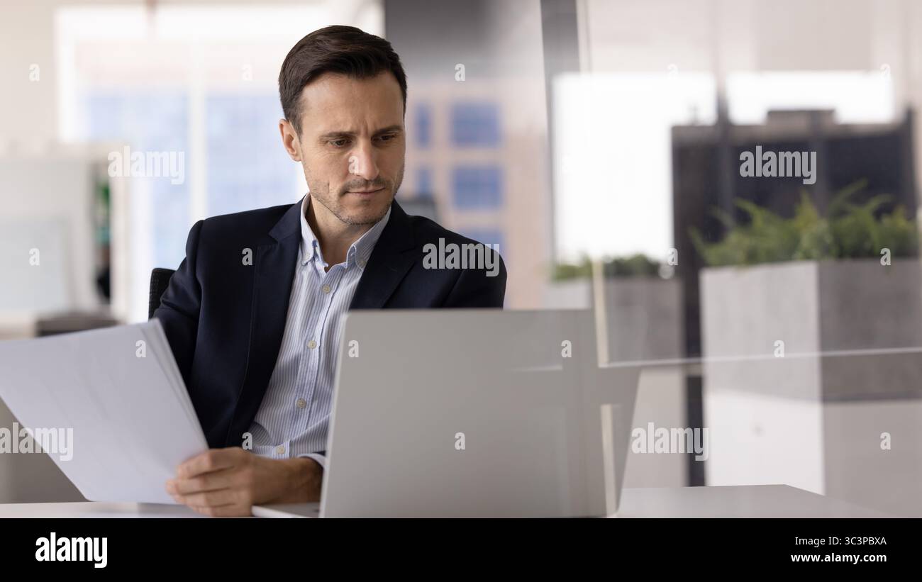 Man engaged in task cross-referencing digital and printed information ...
