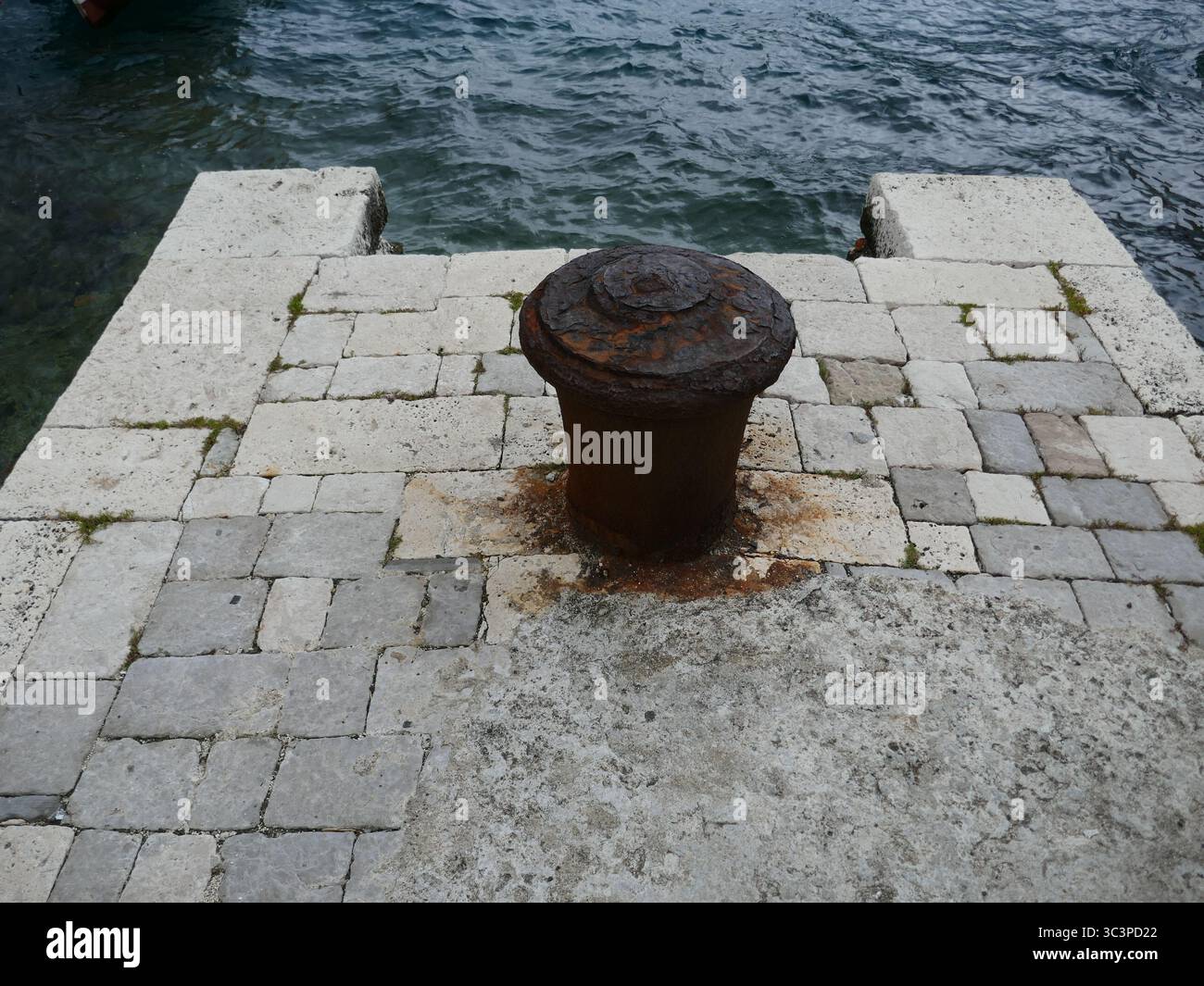Rusty old metal mooring bollard on stone dock with ocean waves off pier ...