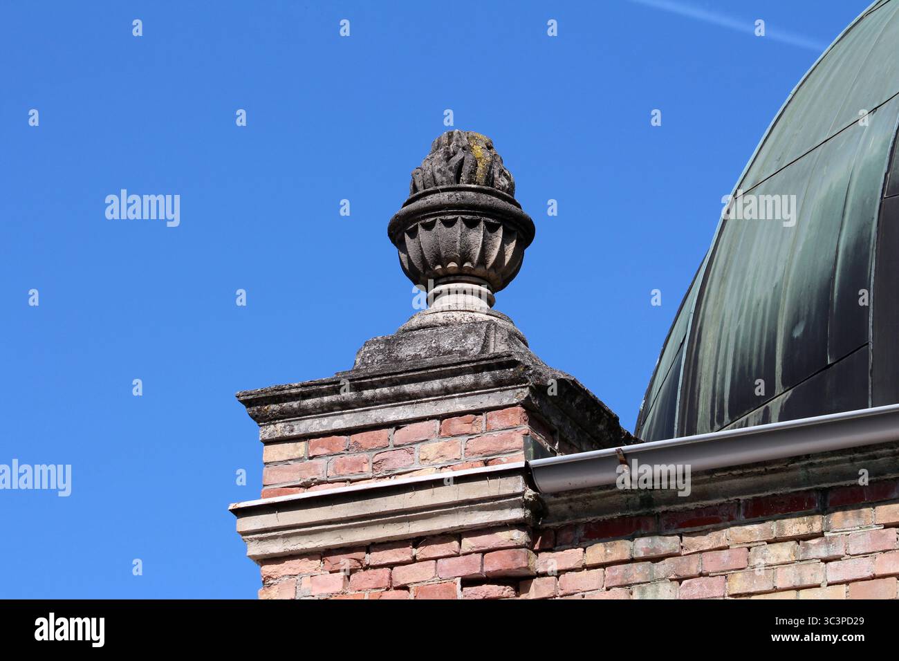 An ornamental stone finial with weathered patina sits atop a brick ...