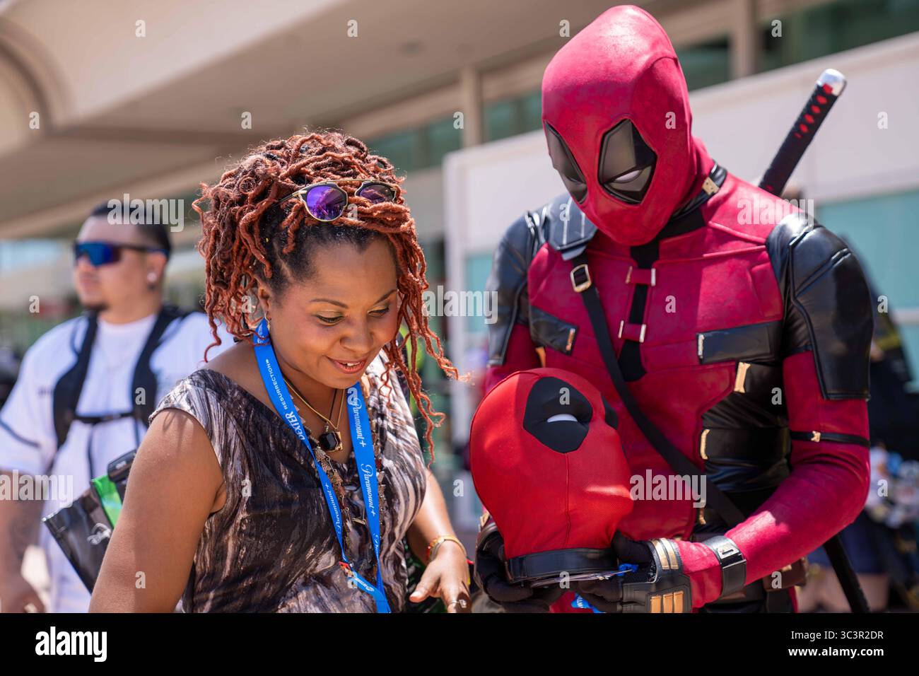 A cosplayer dressed as Deadpool interacts with a fan and playfully ...