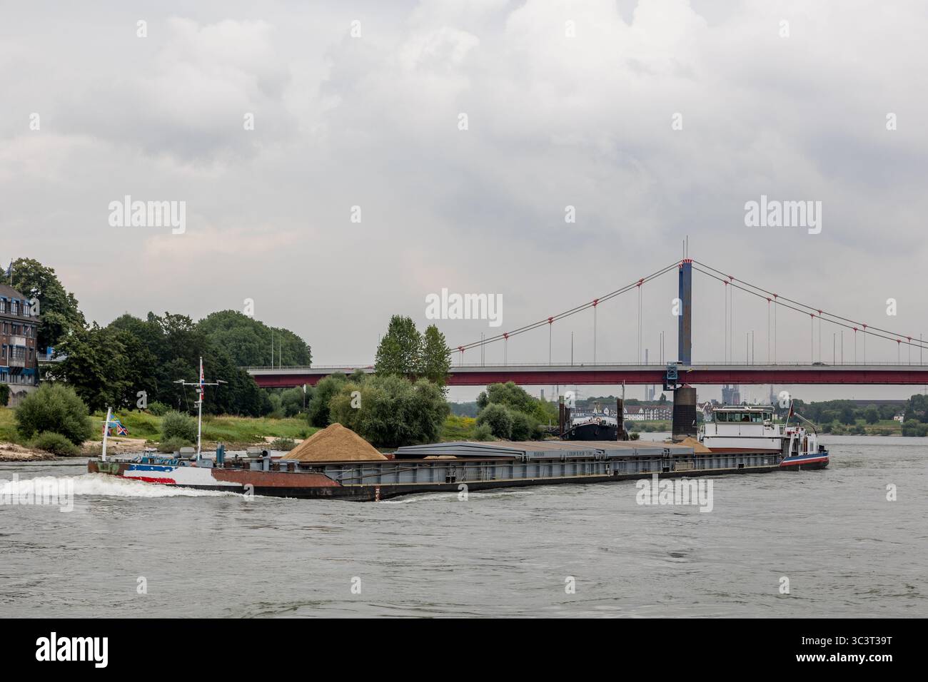 A river barge with sand on rhine river under suspension bridge near ...