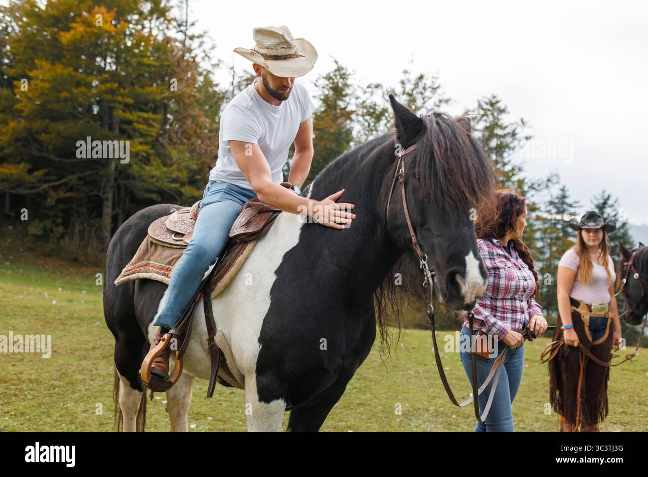 A man in a cowboy hat sits atop a paint horse, petting its neck Stock ...