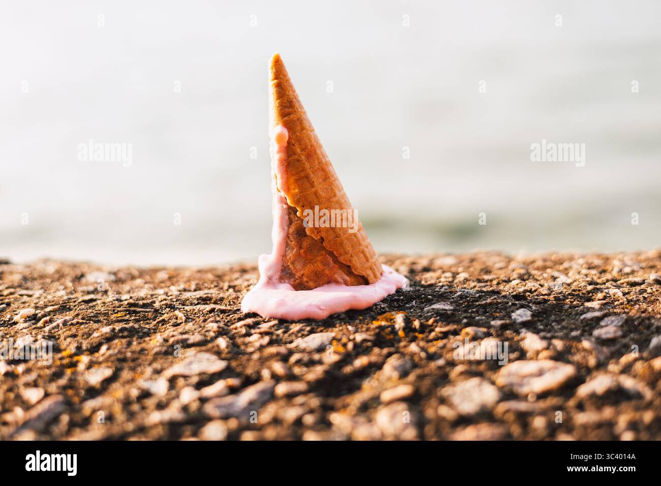Fallen ice cream cone with spilled pink ice cream on a textured ...