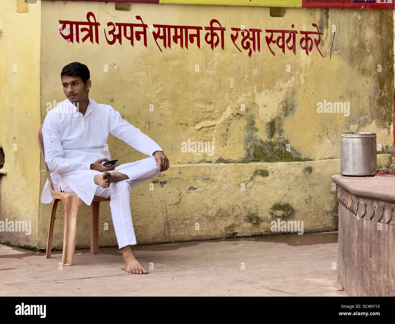 Man in white clothes sitting relaxed at a yellow wall with red Indian ...