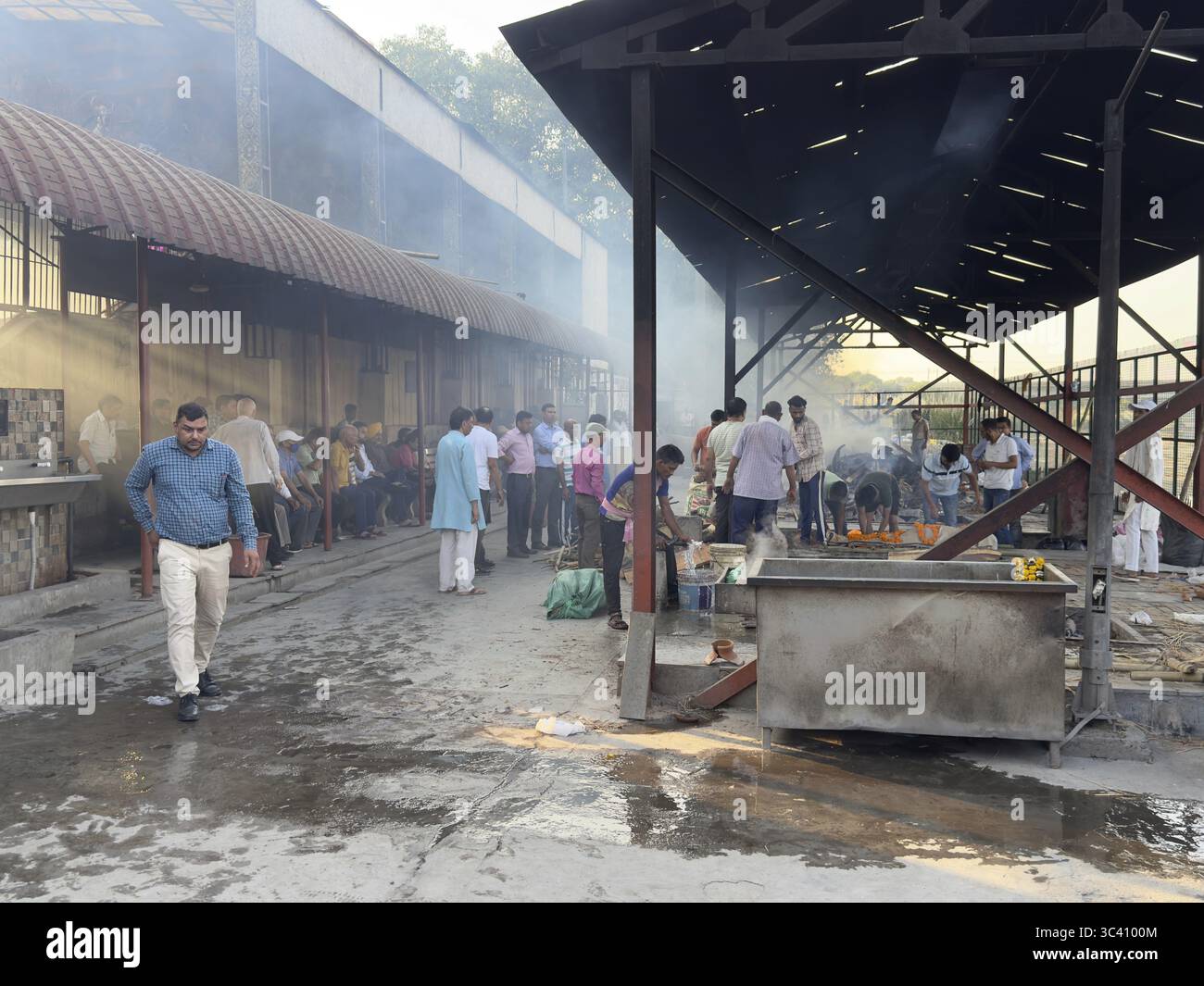 A group of people stand under the metal roofs of a crematorium and ...
