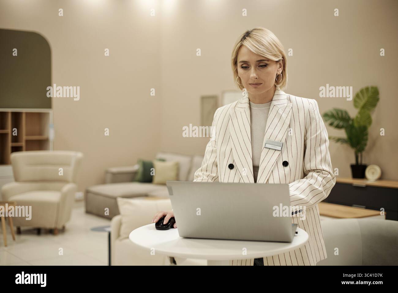 Caucasian young adult woman standing at round table using laptop in ...