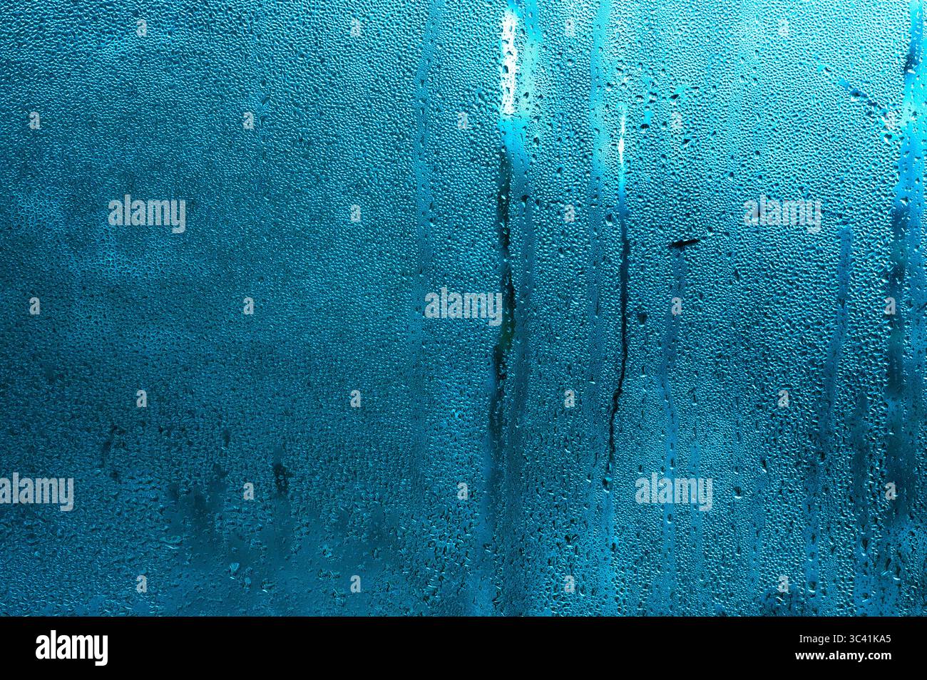 drops slowly sliding down wet window pane, creating winding paths on ...