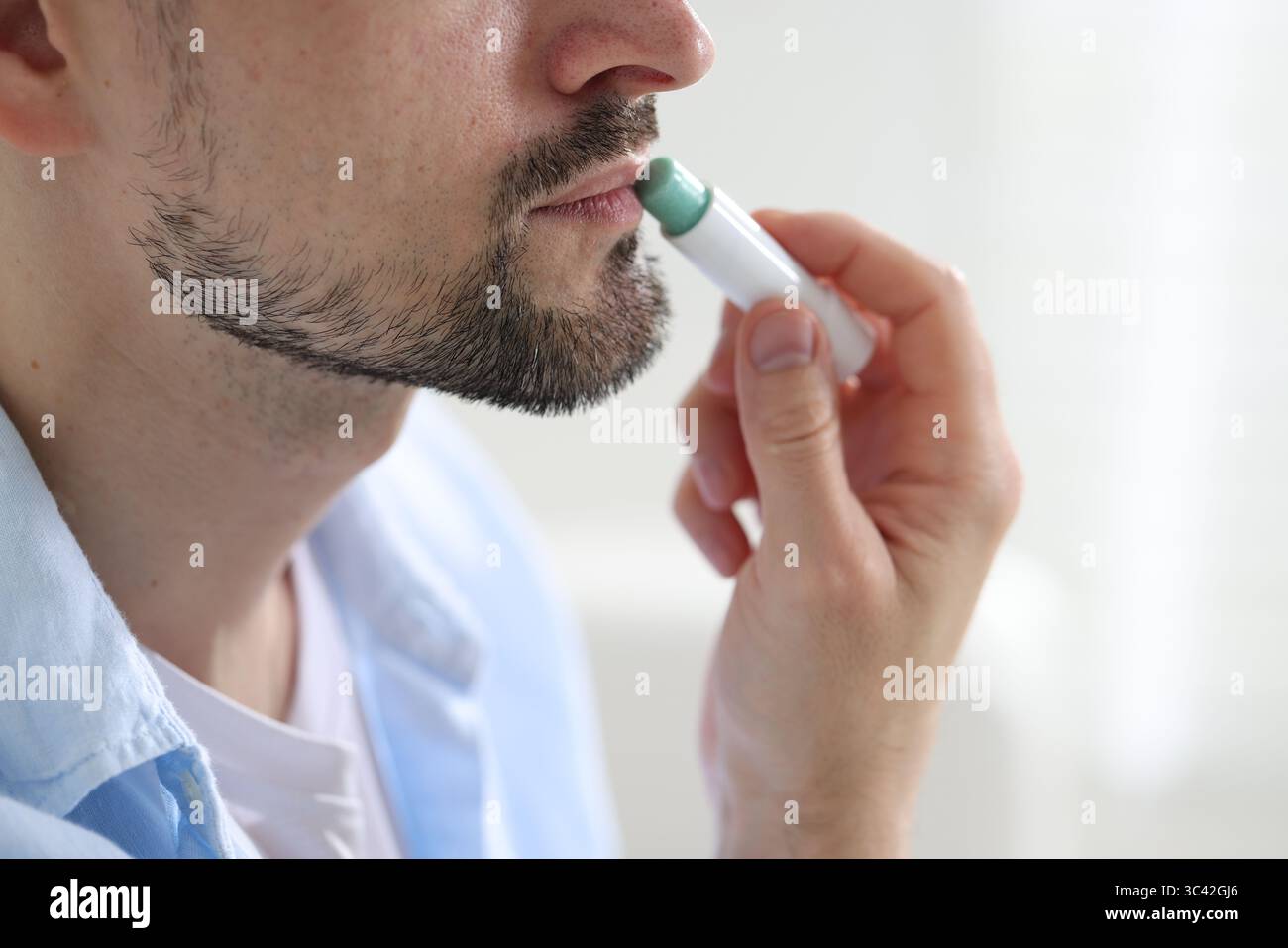 Man applying lip balm onto his lips on blurred light background ...