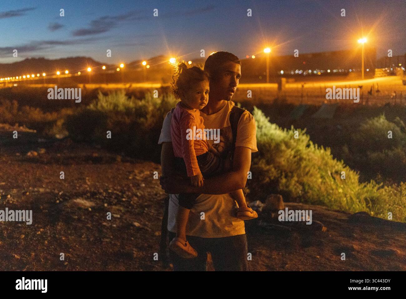 A man cradles a child amidst the dim glow of streetlights on the Ciudad Juarez border ...