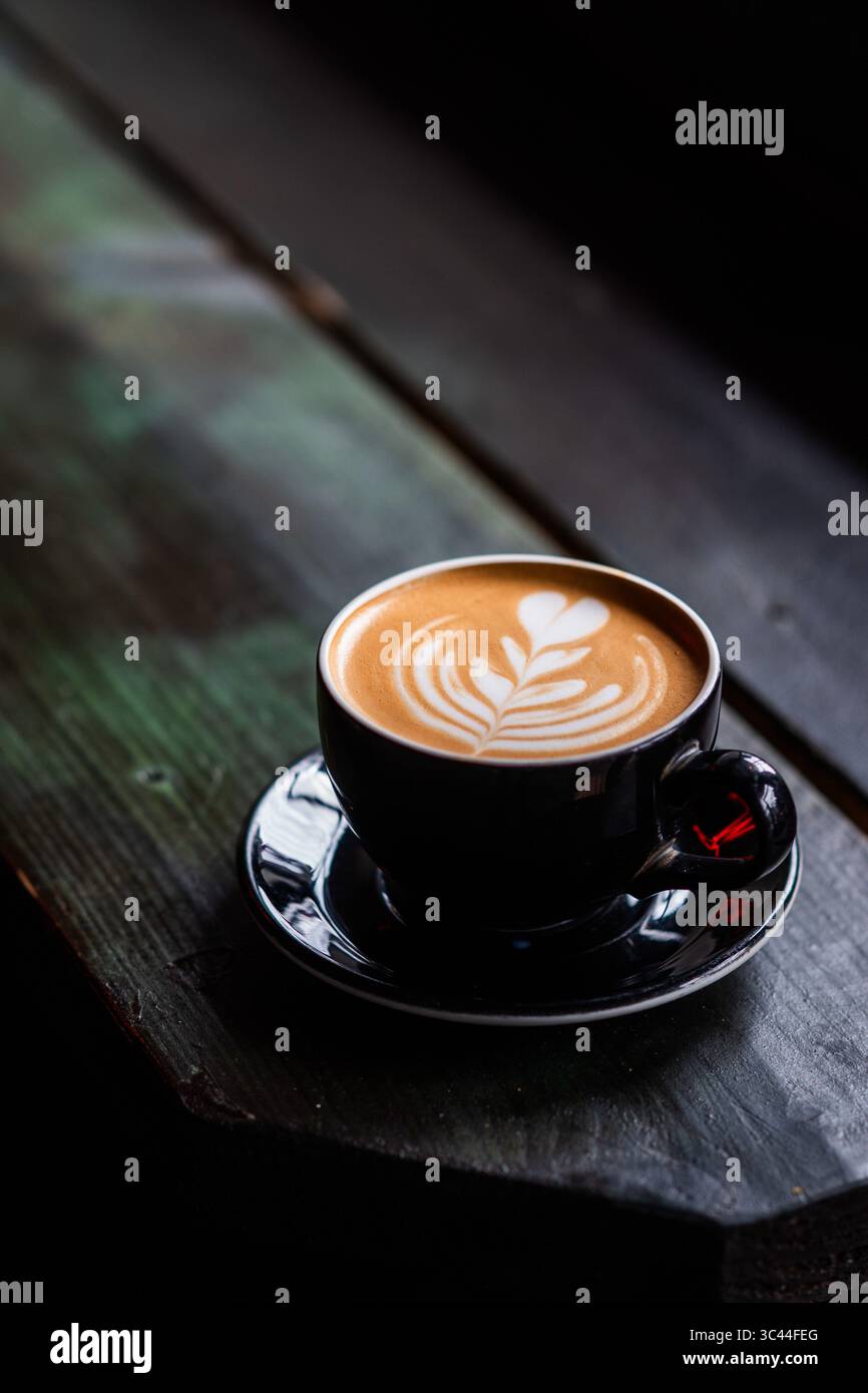 Cup of cappuccino with intricate latte art, served on a rustic wooden table in a cozy coffee ...