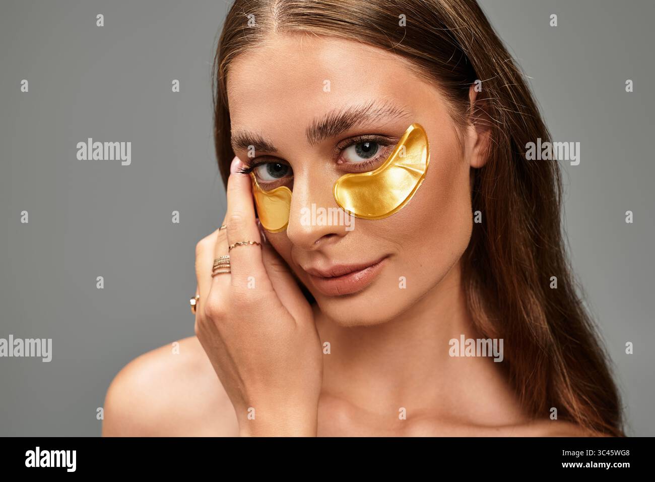 A young woman smiles at the camera while using golden under eye masks ...