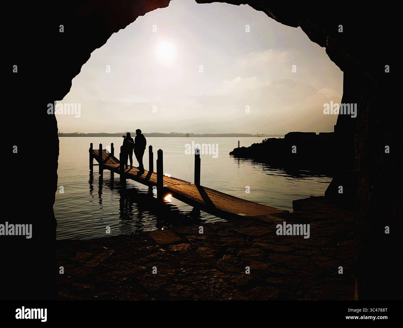 View through stone arch onto Lake Geneva with old wooden pier and two ...
