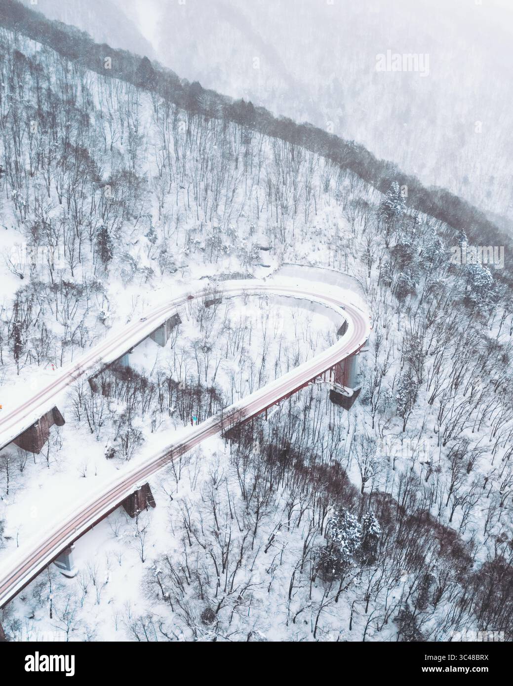 Aerial view of a winding road cutting through a snow-laden forest, the ...
