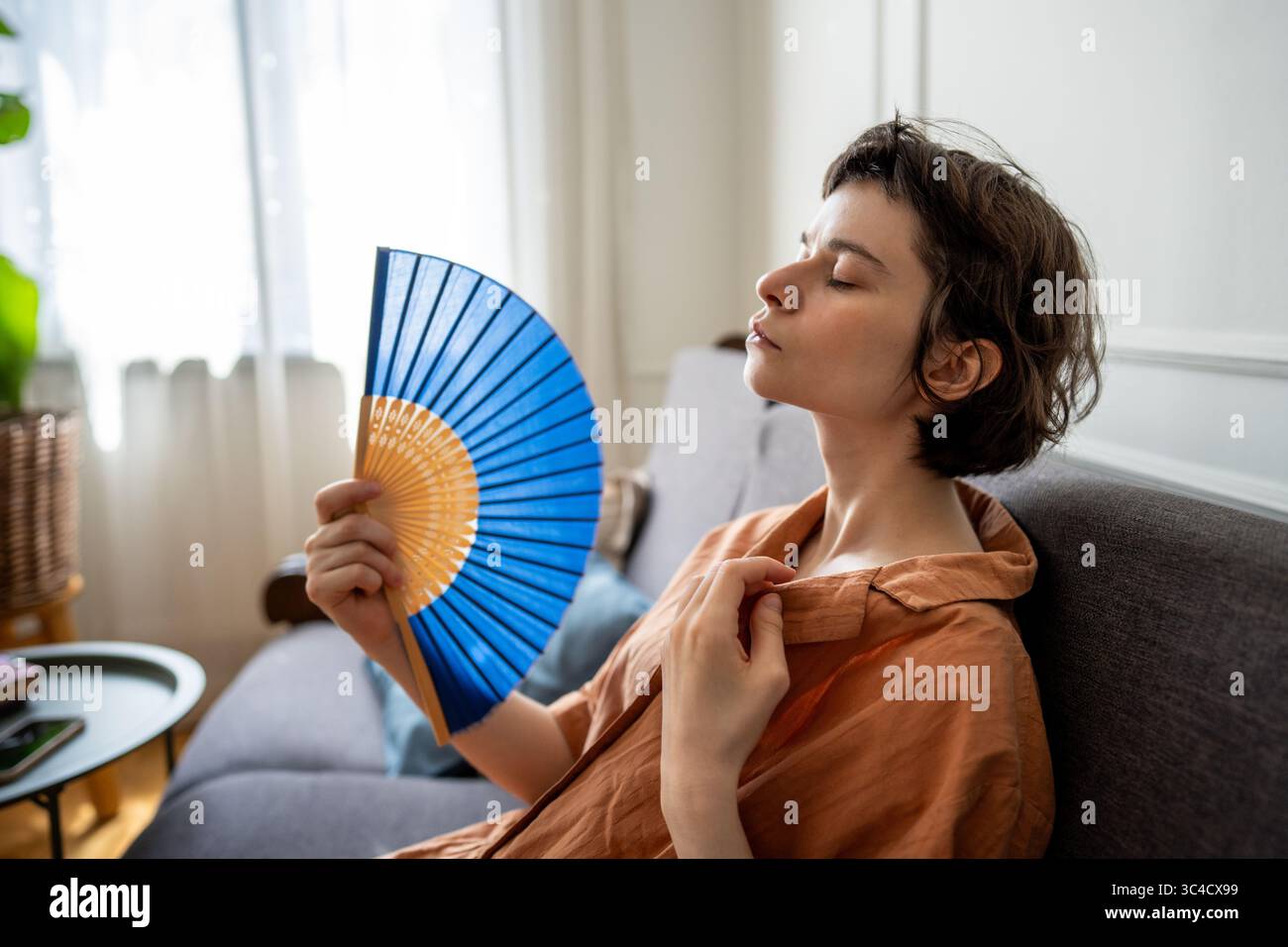 Exhausted sweaty woman fanning herself sitting on sofa suffering from ...
