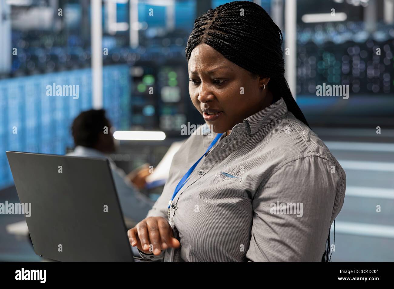 System administrator in server room using laptop to implement and manage data backup solutions ...