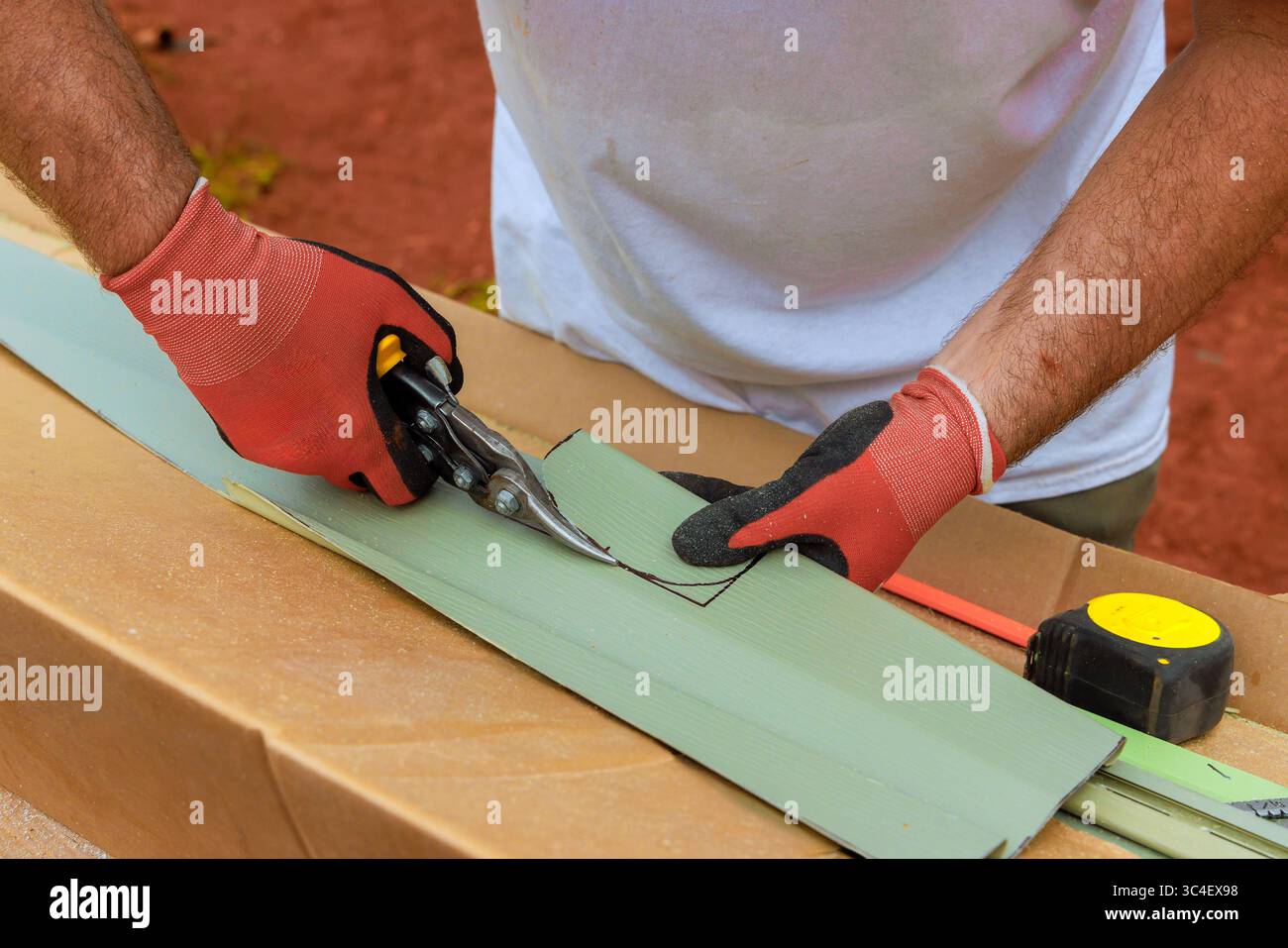 Skilled worker uses scissors to cut green sheet vinyl siding while ...