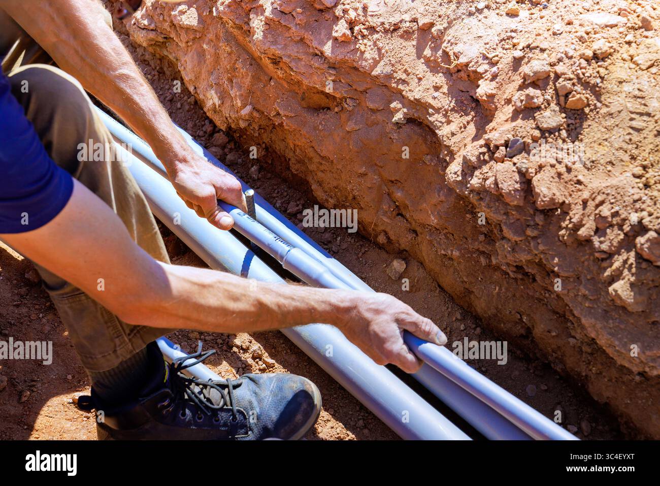 Construction worker carefully positions plumbing pipes into trench on ...