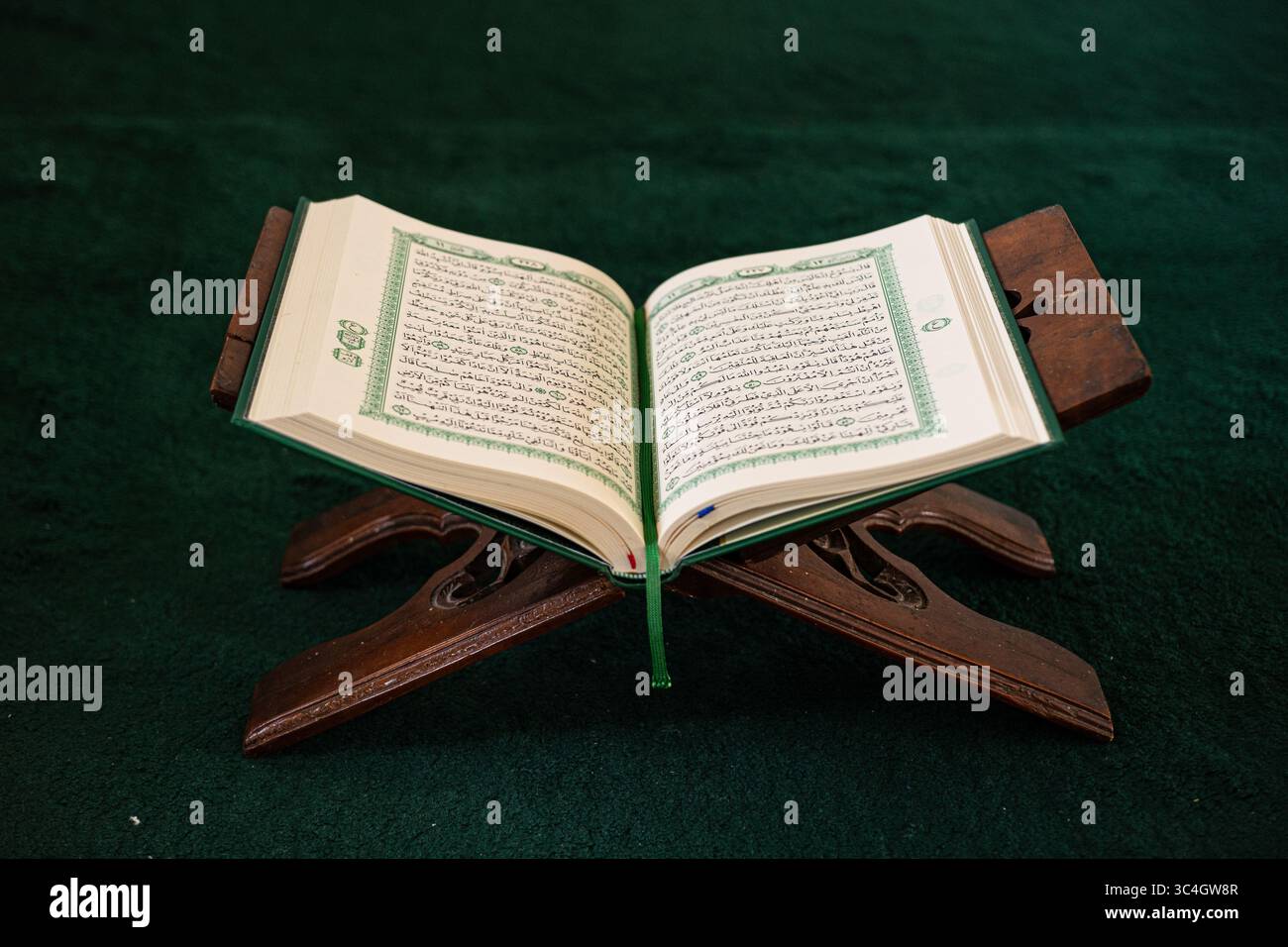 Open Quran on a wooden stand, placed on a dark green prayer rug. Ideal ...