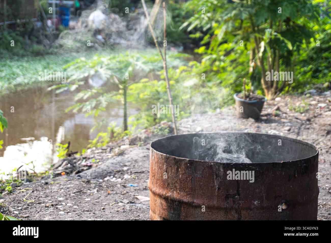 Rusted trash bin with burning garbage, smoke rising, set against a ...
