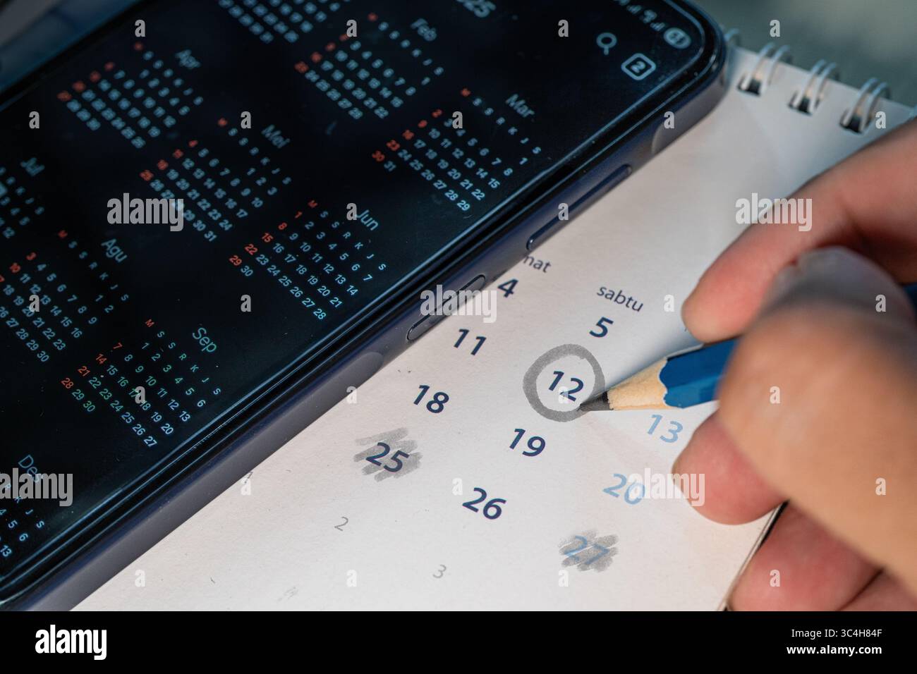 Hand marking important date on paper calendar with pencil, smartphone ...