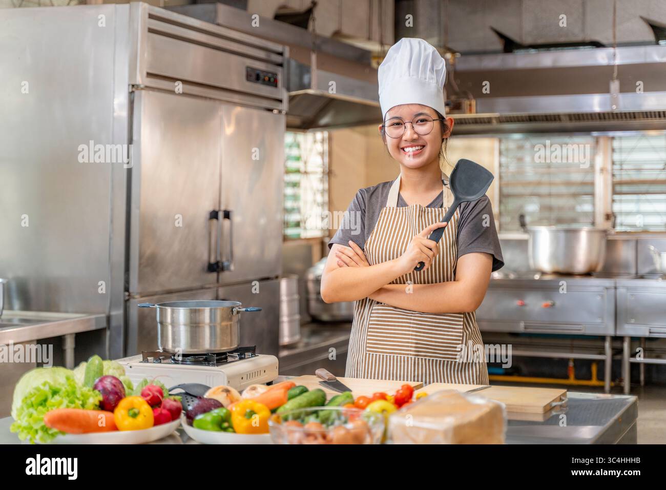 Smiling young female chef in professional kitchen attire, holding a ...