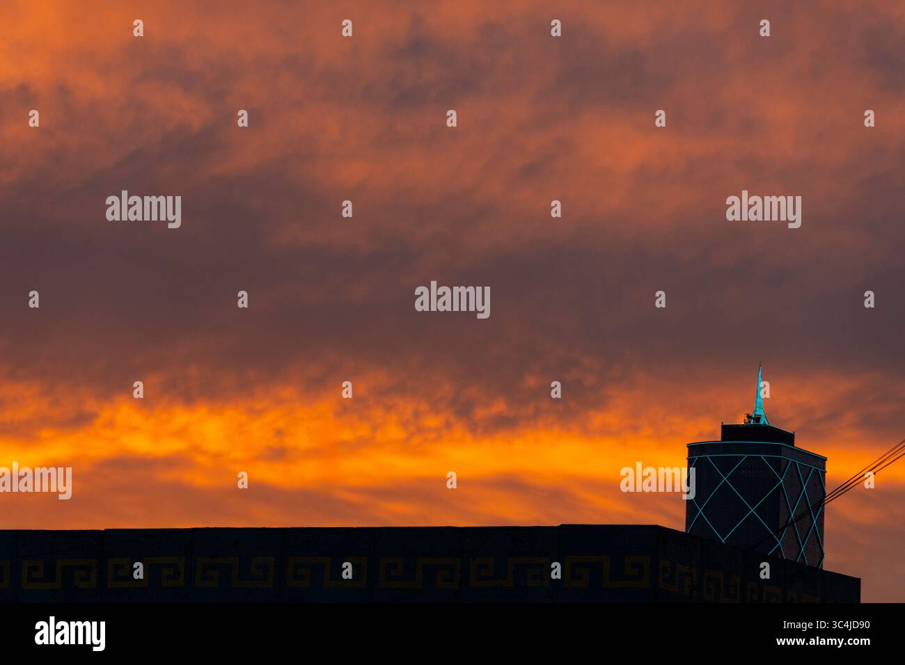 A vibrant orange sunset silhouettes a modern building with a pointed ...