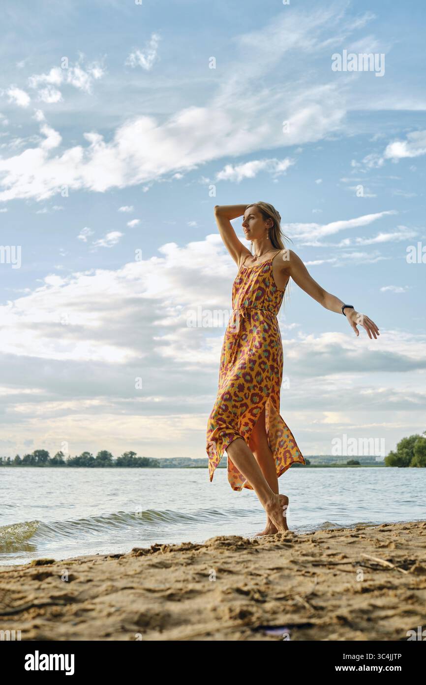 A woman stands barefoot on sandy shores, wearing a bright dress with a ...