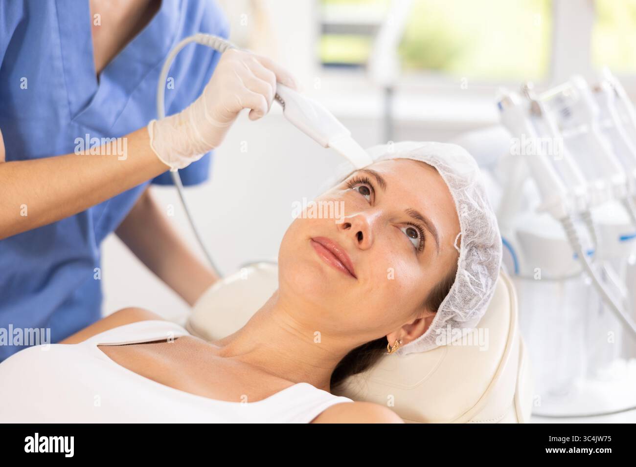 Young female client experiencing facial skin peeling using ultrasonic ...