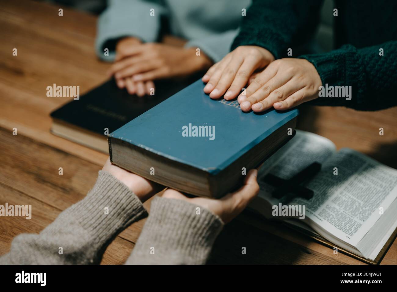 Group of Christians sit together and pray around a wooden table with ...