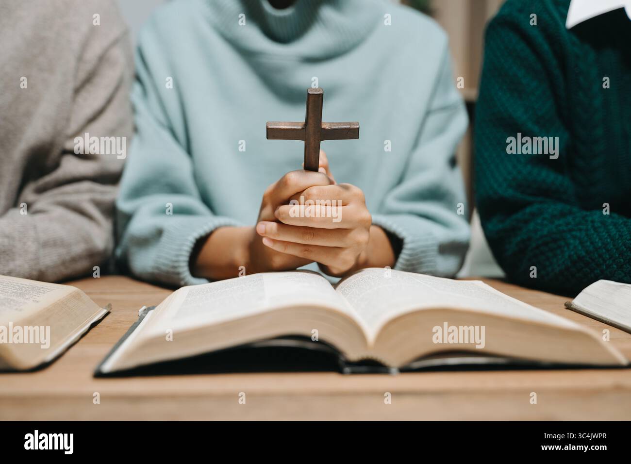 Group of Christians sit together and pray around a wooden table with ...