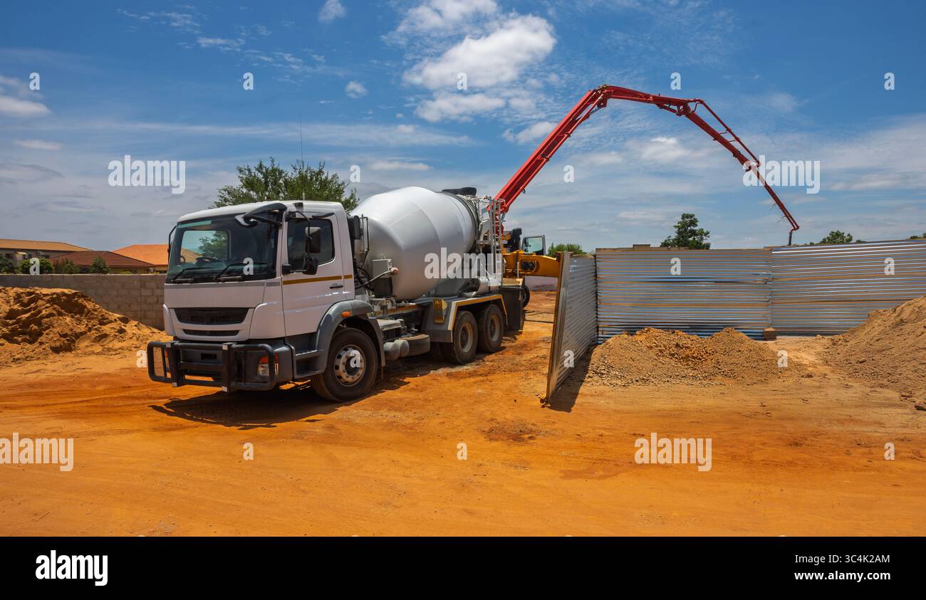White concrete mixer truck with red boom pump arm pouring concrete ...