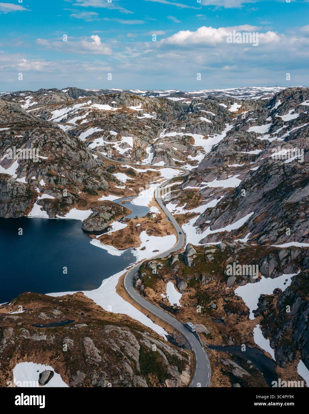 Aerial view of a winding road snaking through a rugged, snow-dusted landscape with a dark lake ...