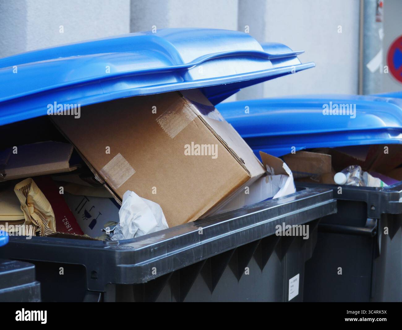 Blue trash can is full of trash, including a box and a roll of toilet ...