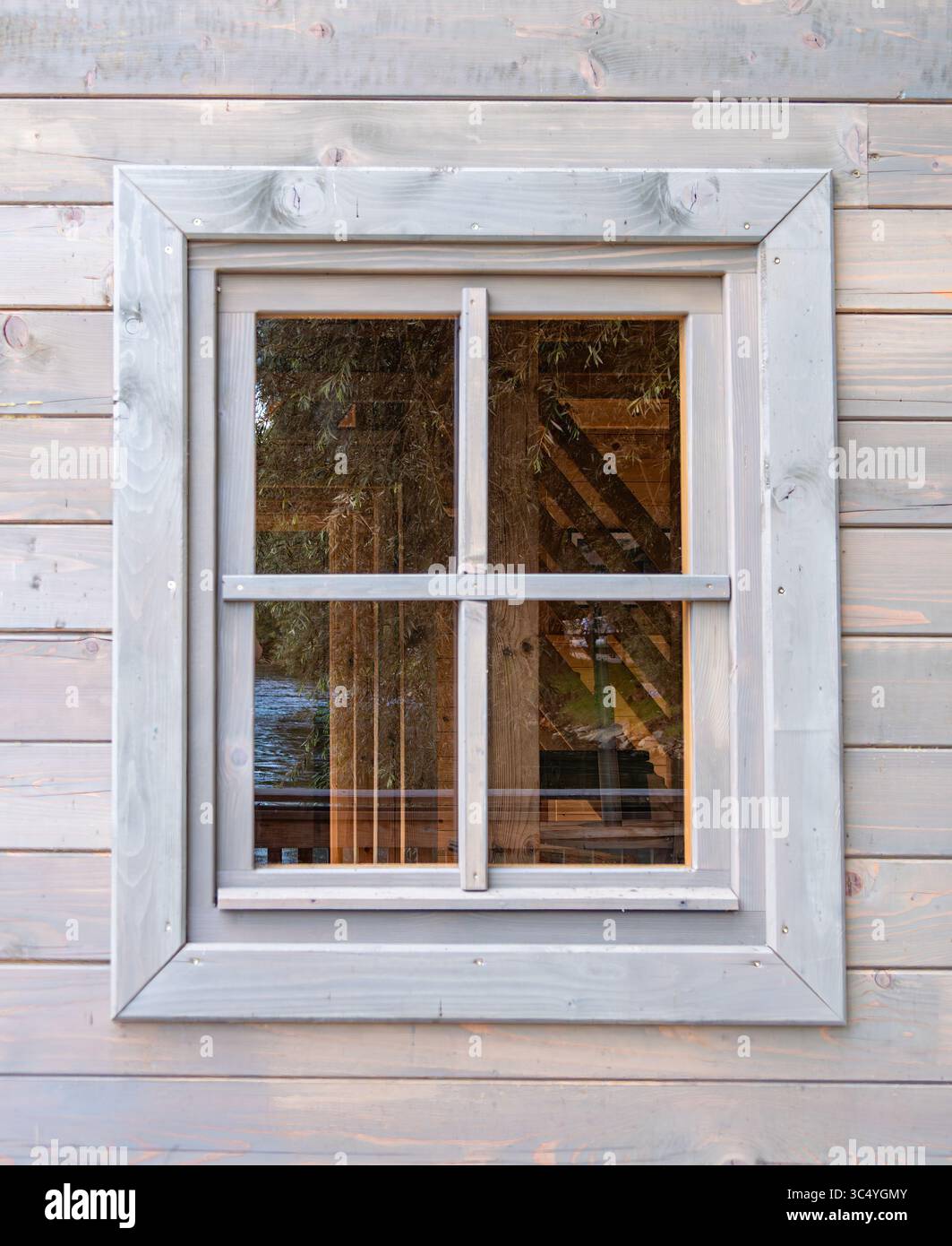 A wooden window frame with a grid pattern, reflecting trees and a ...