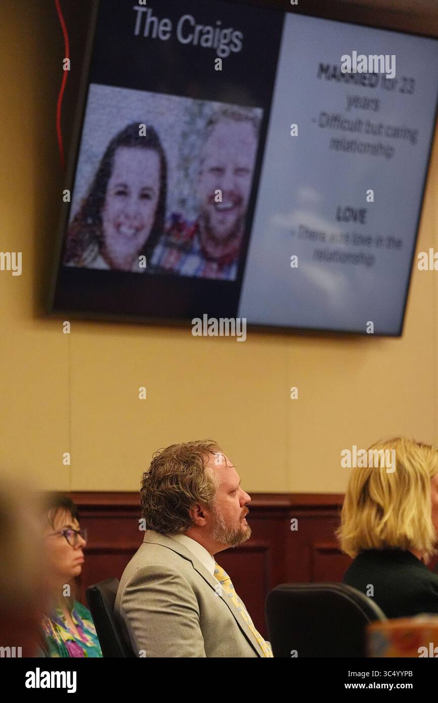 James Craig sits under an image on a screen of the dentist and his wife ...