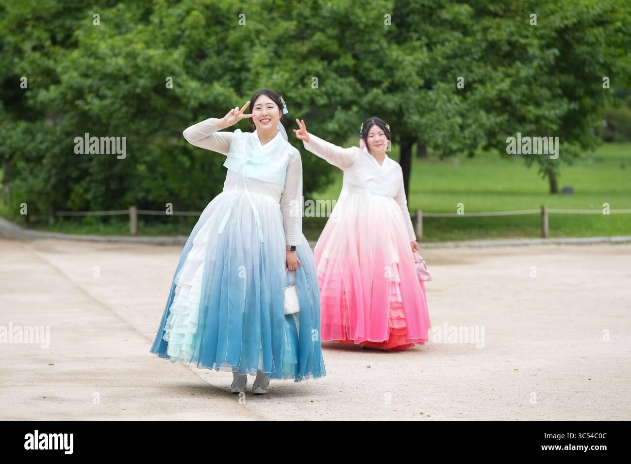 Two Korean women in their twenties walk together through a lush green ...
