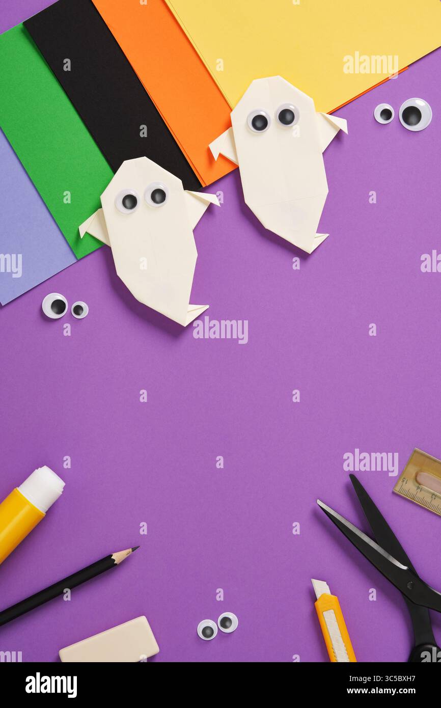 Origami paper ghosts with googly eyes with craft supplies on a purple ...