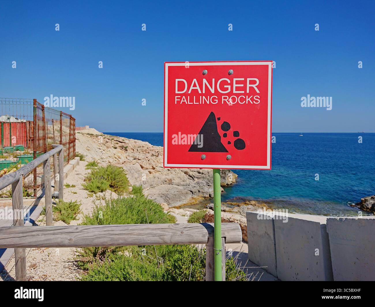 Red danger sign warning of falling rocks near seaside cliff with blue ...