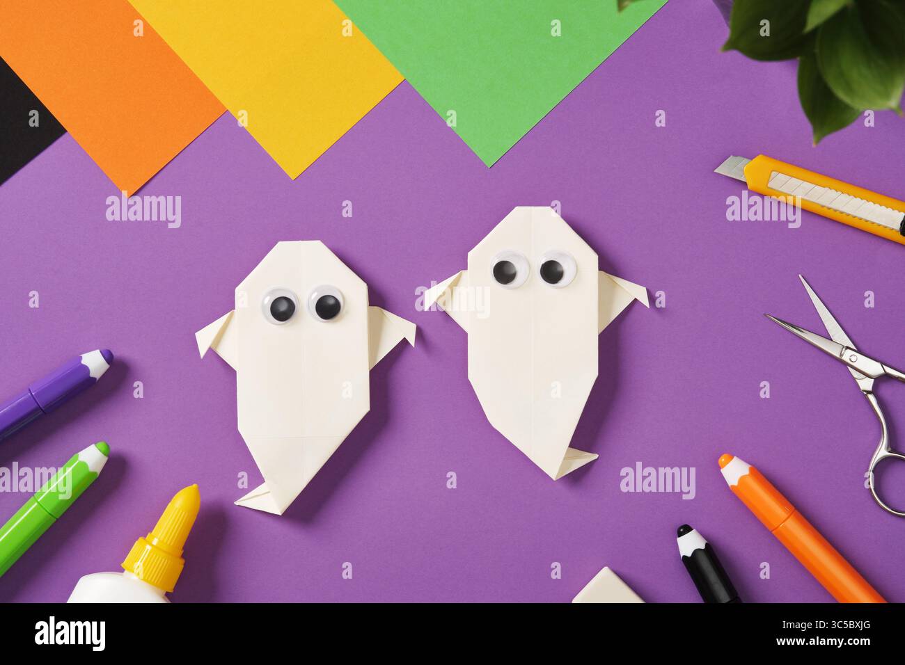 Origami paper ghosts with googly eyes surrounded by colorful craft ...