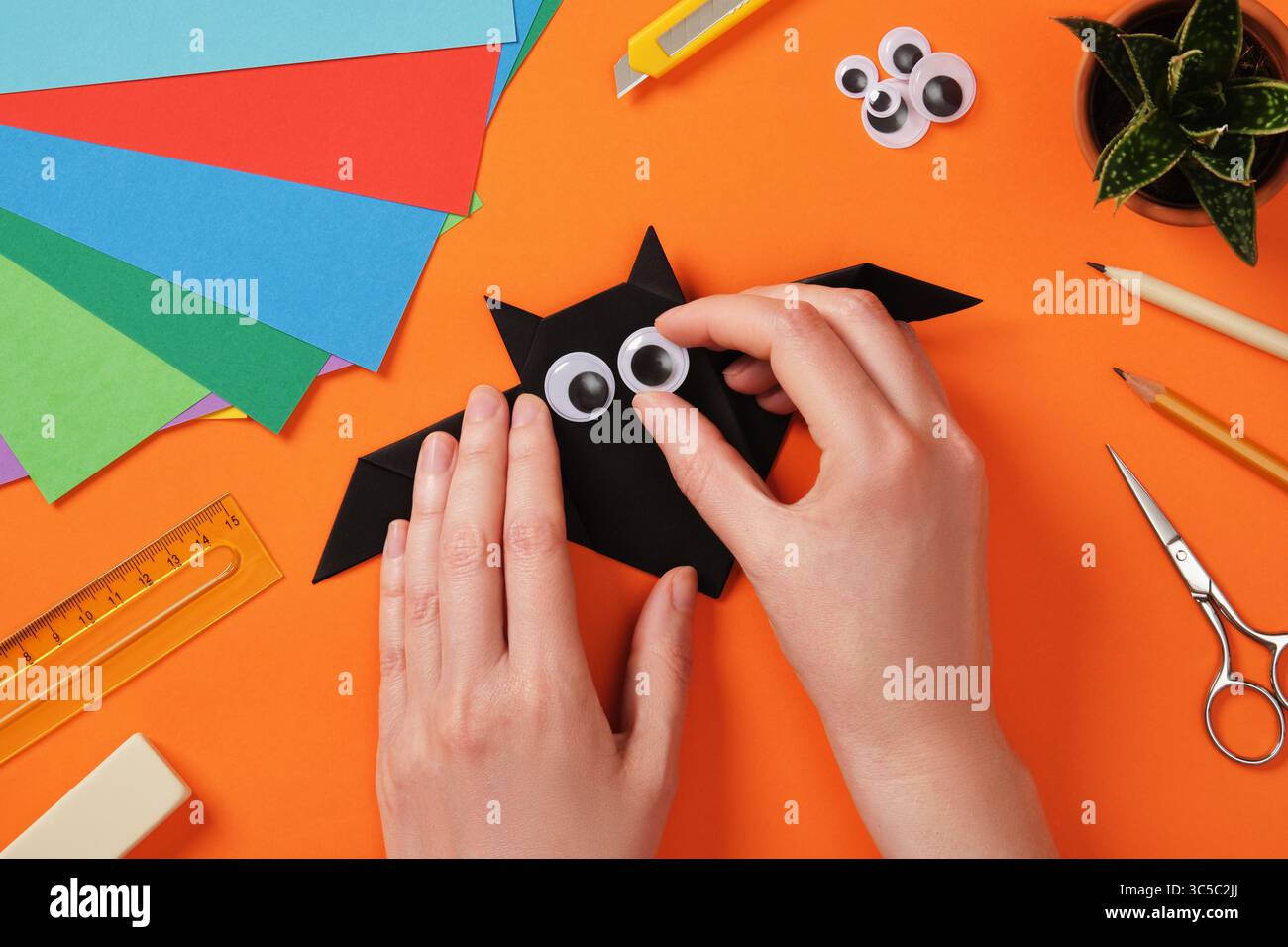 Making an origami bat paper craft. Women's hands attach an eye to a ...