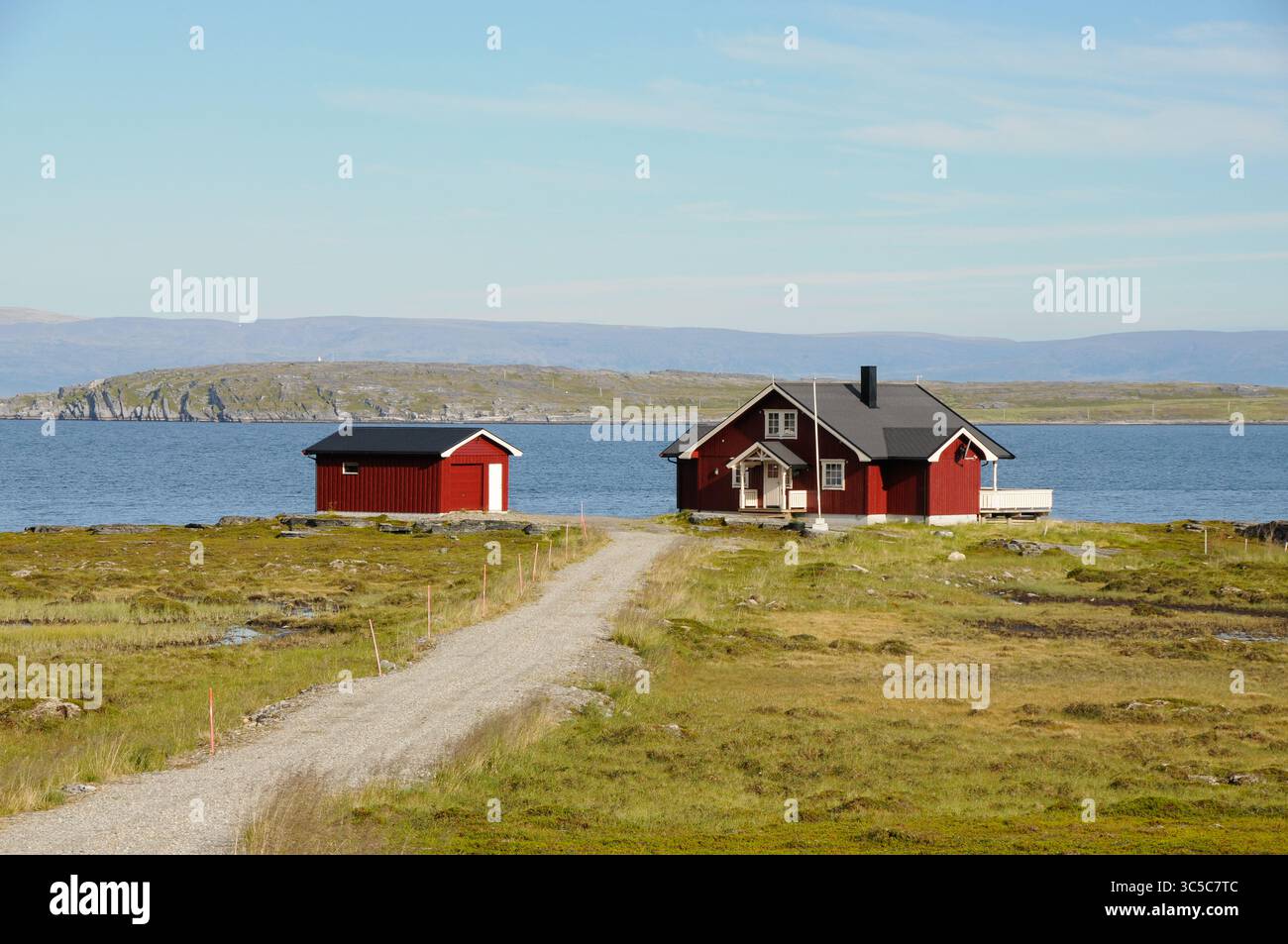 Red wooden house and shed on the remote Norwegian coast path to the sea ...